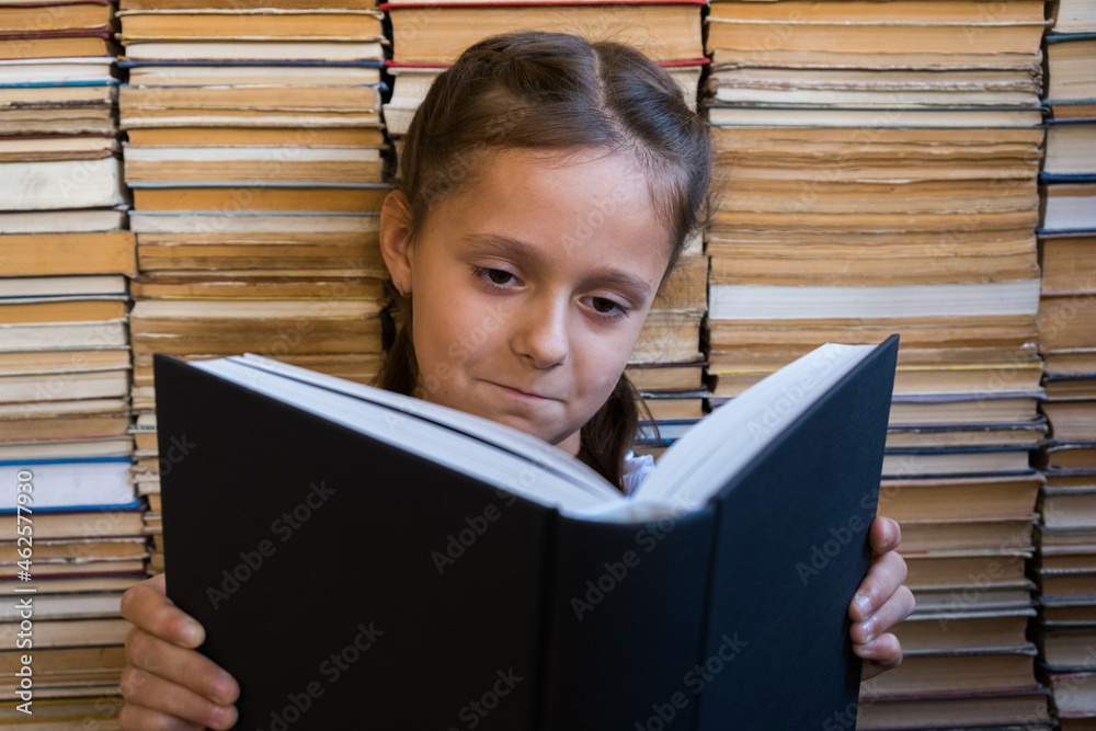 Curious cute preschool kid girl sitting with a book, on books ...
