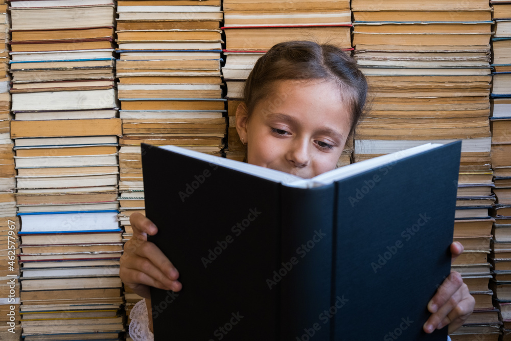 Curious cute preschool kid girl sitting with a book, on books ...