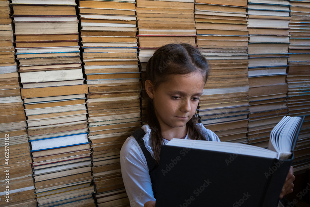 Curious cute preschool kid girl sitting with a book, on books ...
