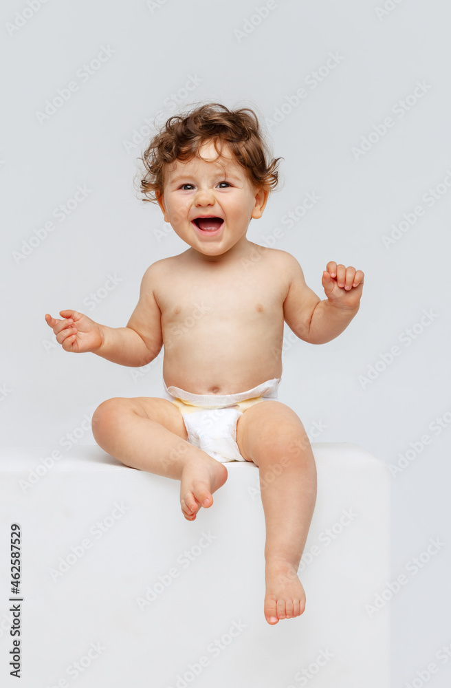 Vertical portrait of little cute toddler boy, baby in diaper joyfully sitting and laughing ...