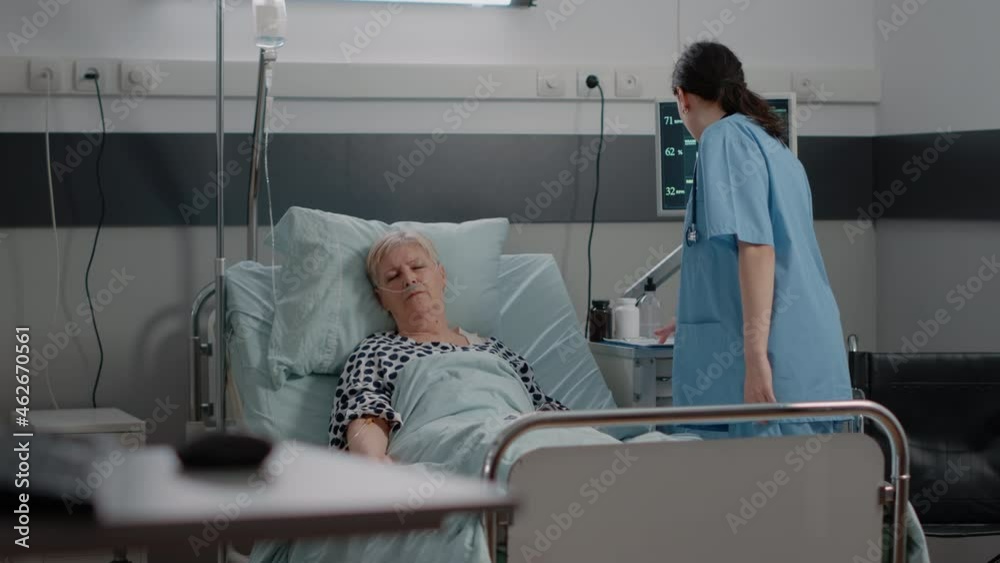 Aged patient with illness resting in hospital ward bed while nurse ...