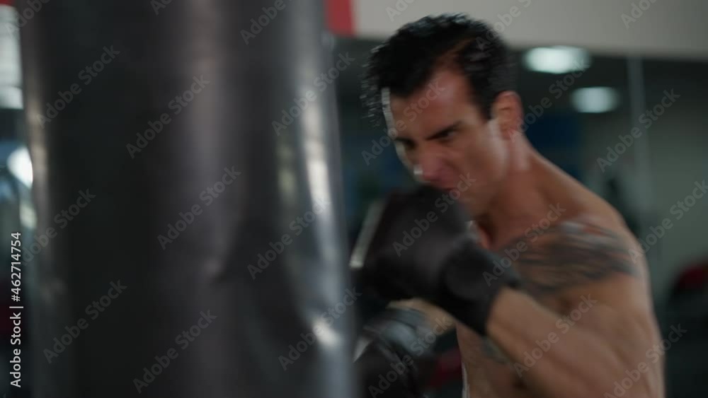 Live camera spinning as concentrated angry boxer hitting punching bag ...