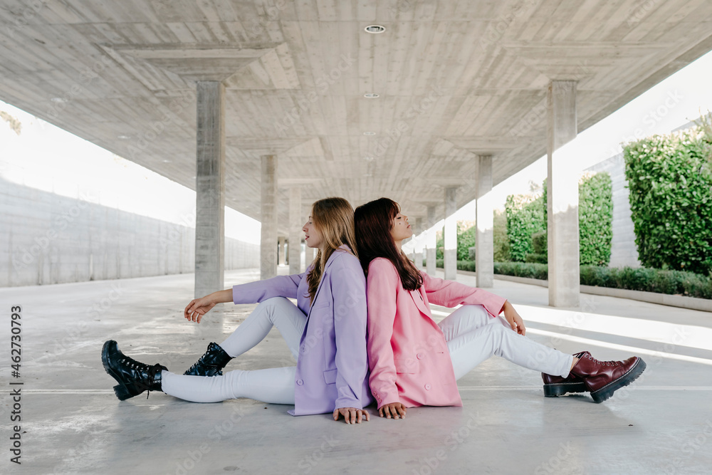 Young sisters sitting back to back on floor at parking lot Stock Photo ...