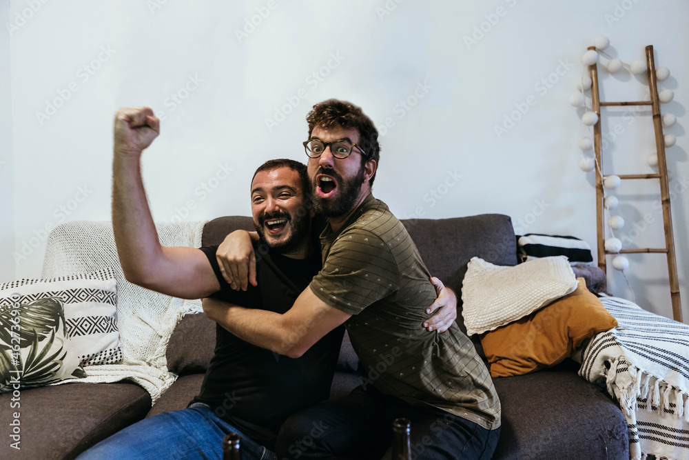 Excited male spectators screaming while watching sports in living room ...