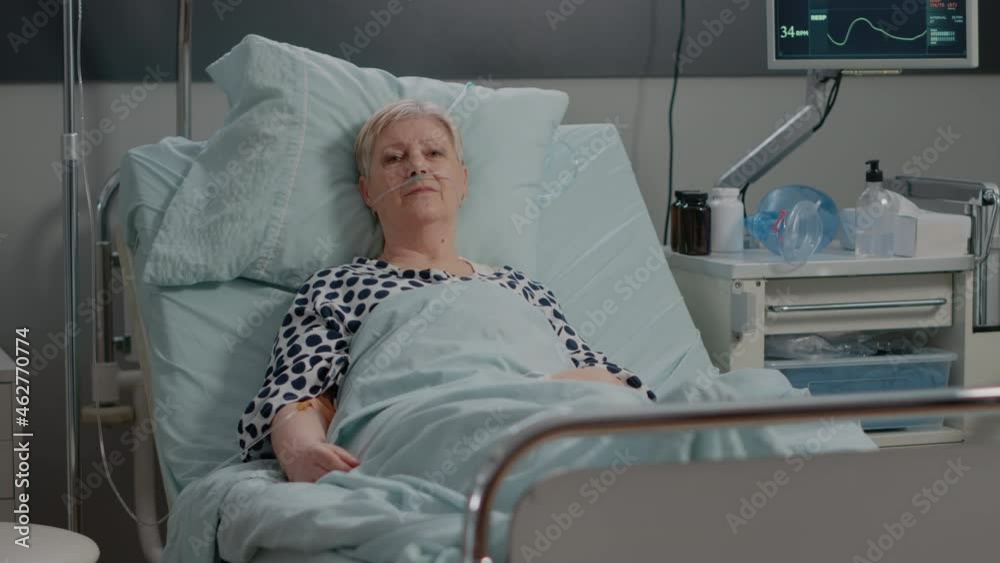 Portrait of sick patient laying in hospital ward bed, looking at camera ...