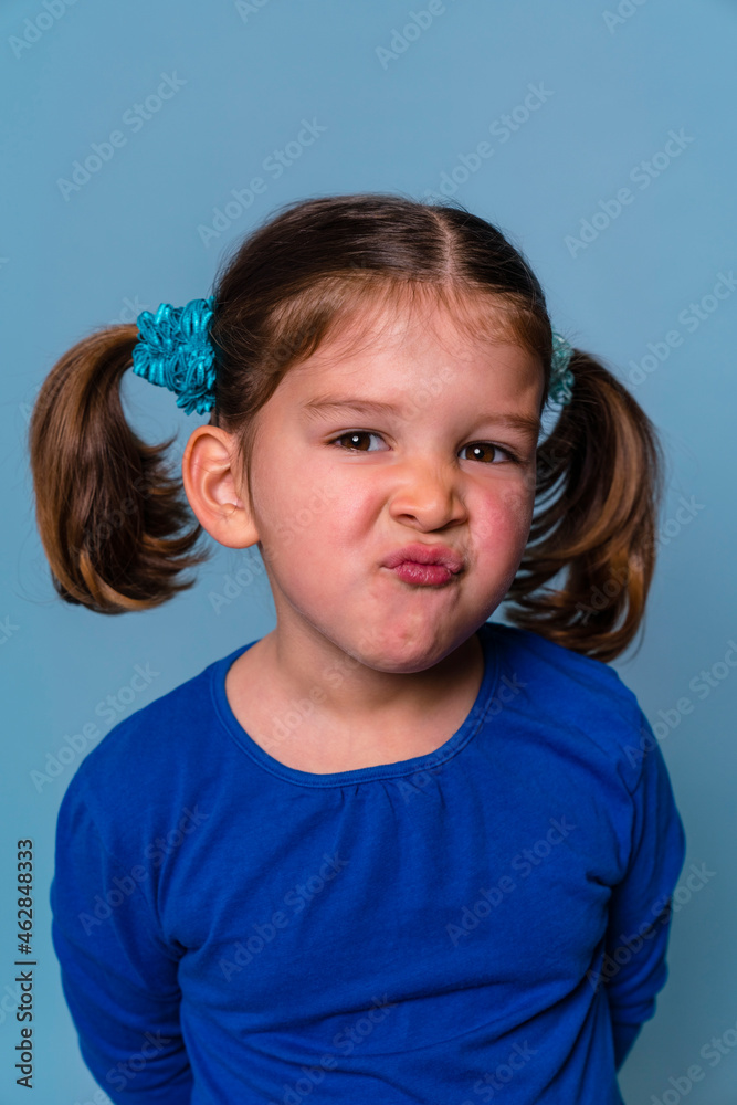 Girl making angry puckering face while standing against blue background ...