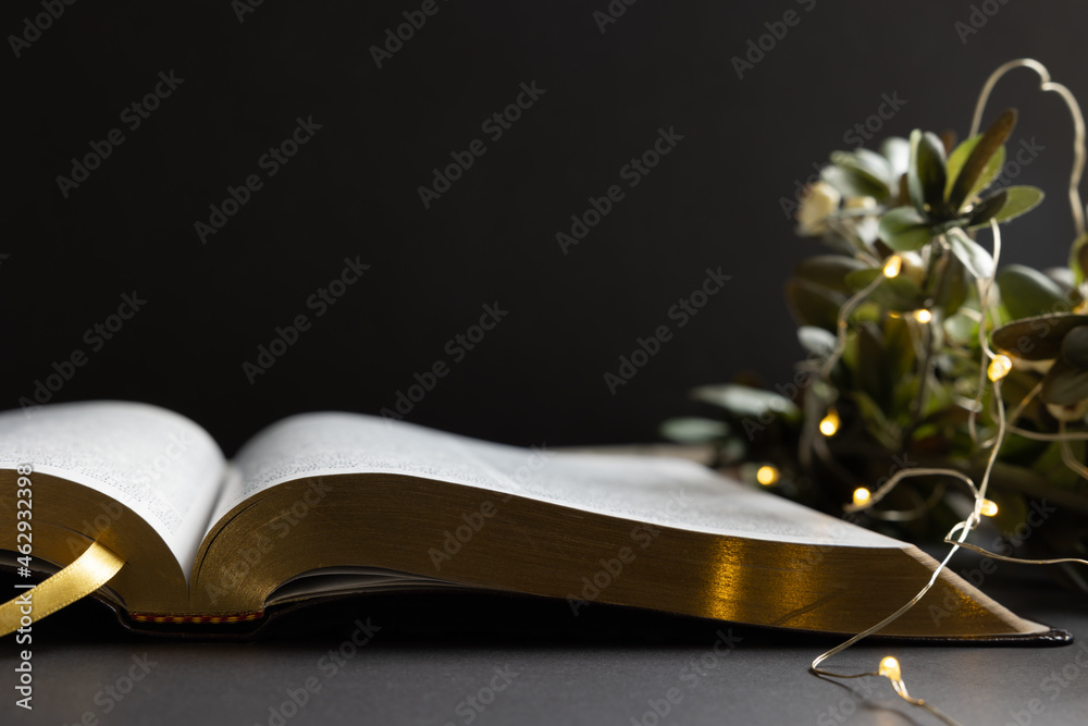 open bible with border of green branches and christmas lights on a ...