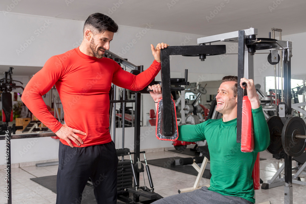 gym teacher teaching a student to do their exercises and train in a gym ...
