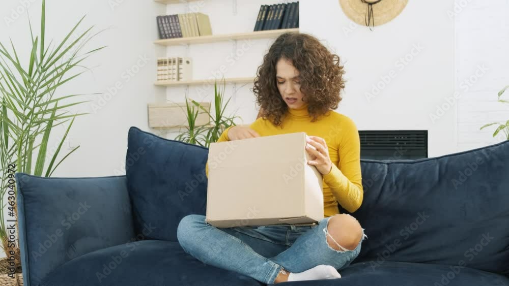 Disappointed young woman unpacking huge carton box, looking inside ...