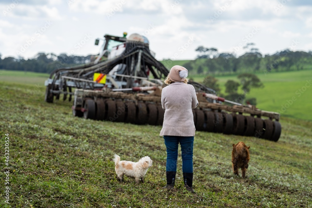 Mother watching son, while he is sowing a crop in a tractor on a farm ...