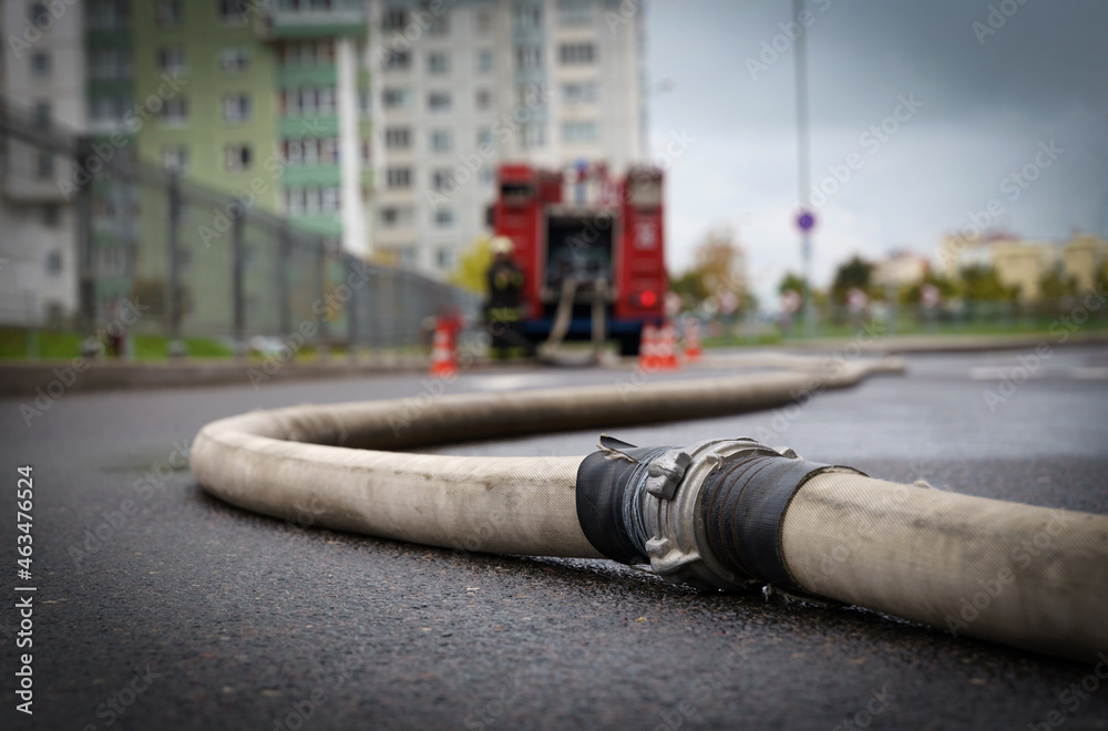 Against the background of a blurred fire truck, a fire hose is ...