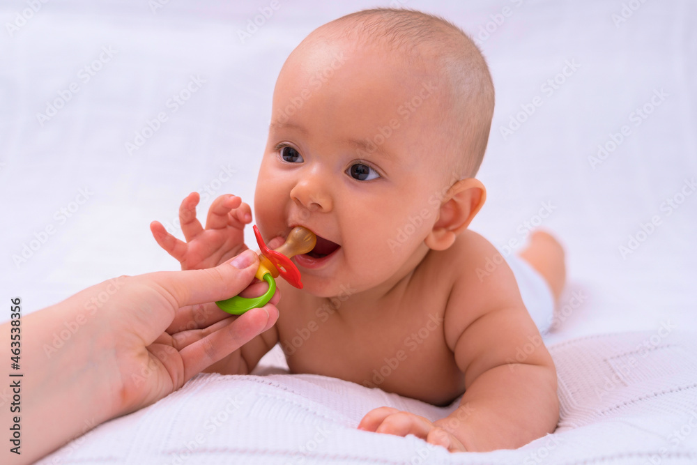 A newborn baby takes a pacifier from her mother's hands while lying on ...