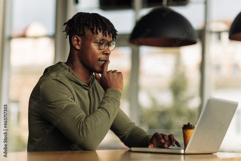 handsome African American man is typing on a laptop while sitting in a ...