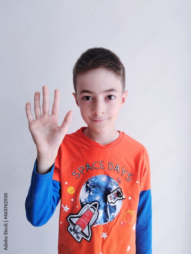 Young boy in orange shirt shows hand up five fingers greeting sign ...