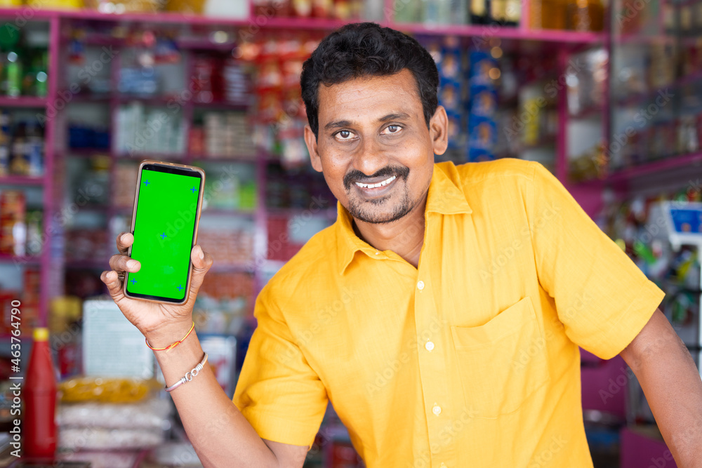 Smiling Merchant at groceries store hold mobile with green screen mock ...