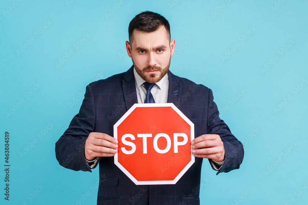 Concerned serious man wearing official style suit holding red stop sign ...