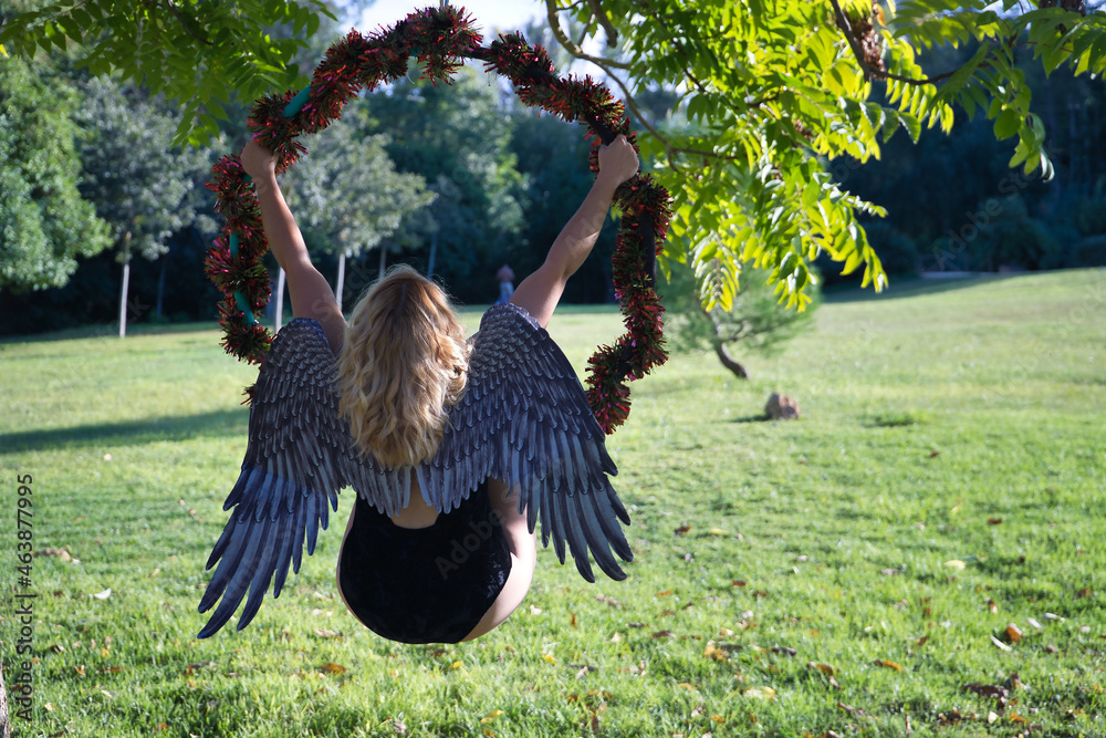 Young blonde woman in a black dress with angel wings hanging backwards ...