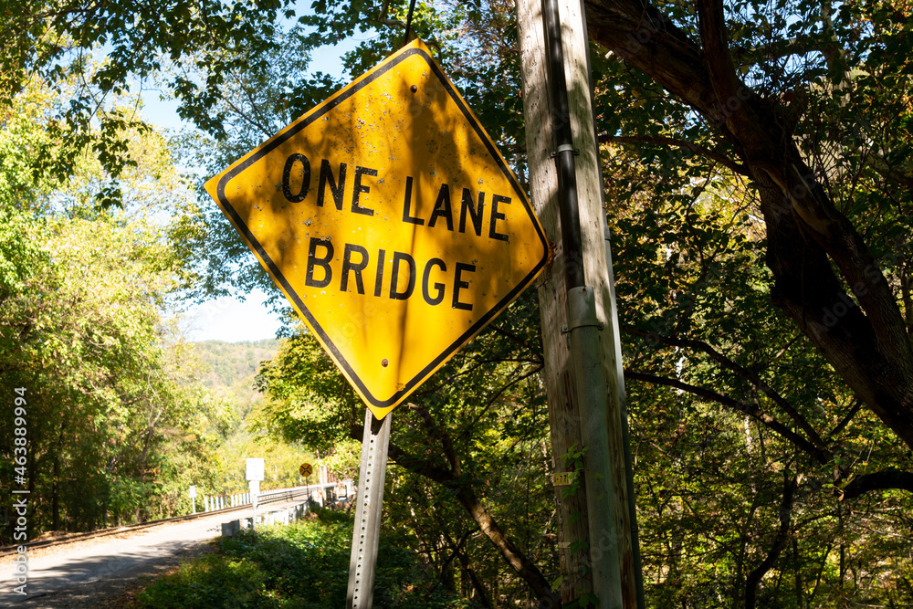 Yellow diamond metal waring traffic road sign reads one lane bridge to ...