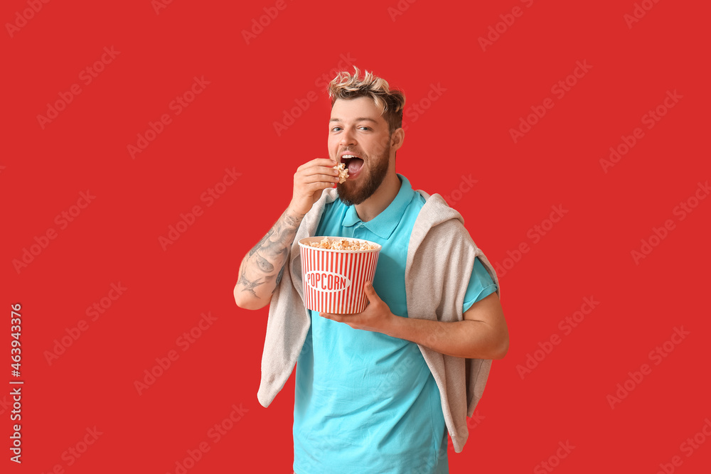 Smiling young guy eating popcorn on color background Stock Photo ...