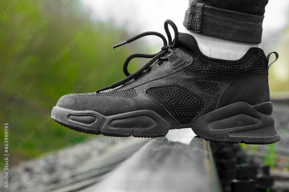sneaker on an iron rail. girl stands with her foot on the railroad ...