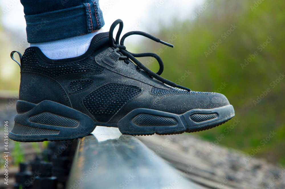 sneaker on an iron rail. girl stands with her foot on the railroad ...