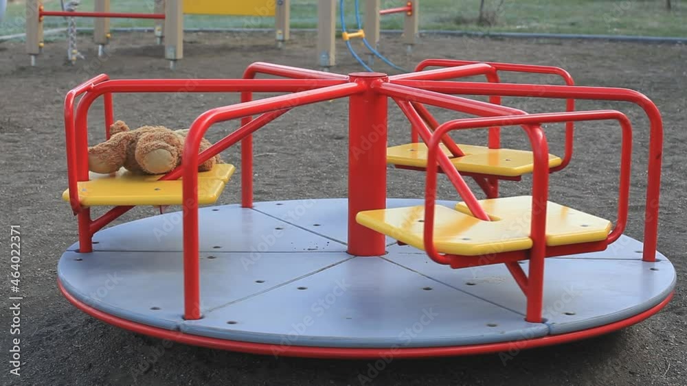 An empty childrens carousel with a brown teddy bear slowly rotates on ...