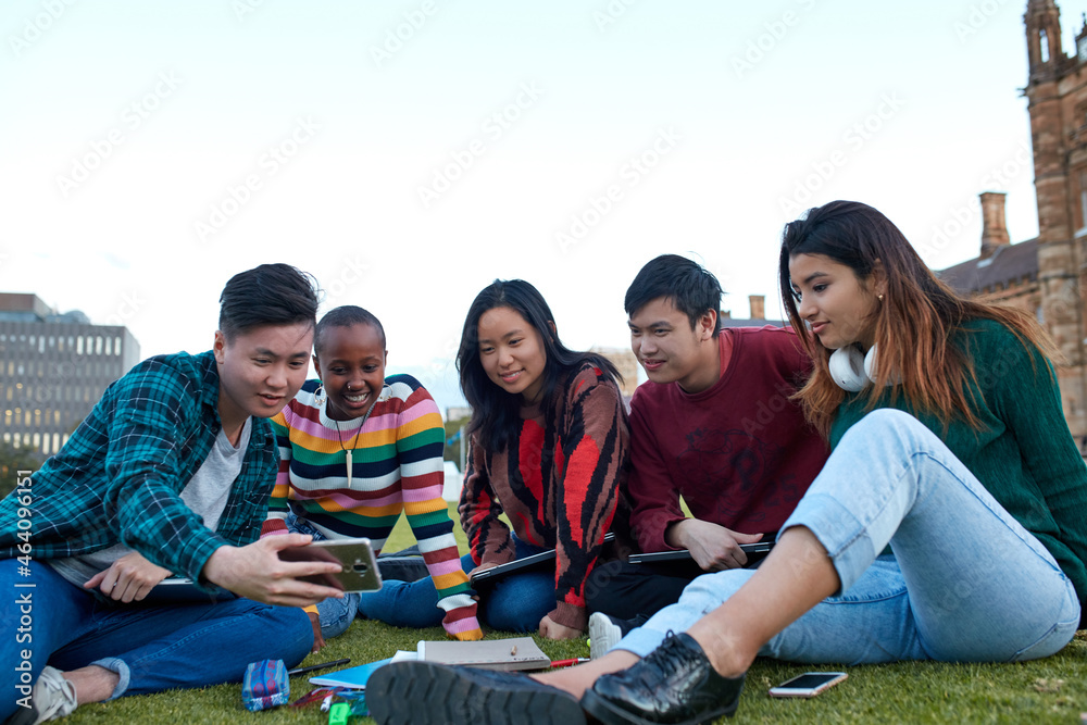 Group of young university students hanging out sitting on grass ...