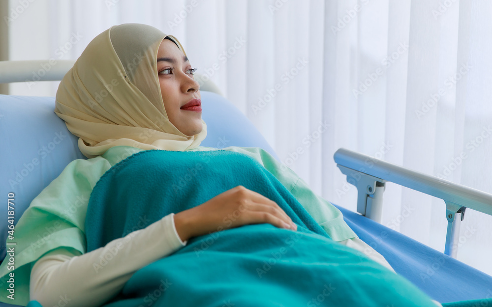 Portrait of sick young female Asian Muslim patient lying on hospital ...