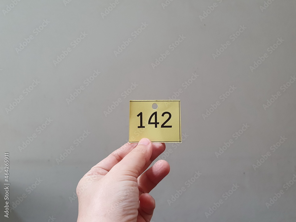 Left hand holding queue ticket number 142 printed in black ink on ...