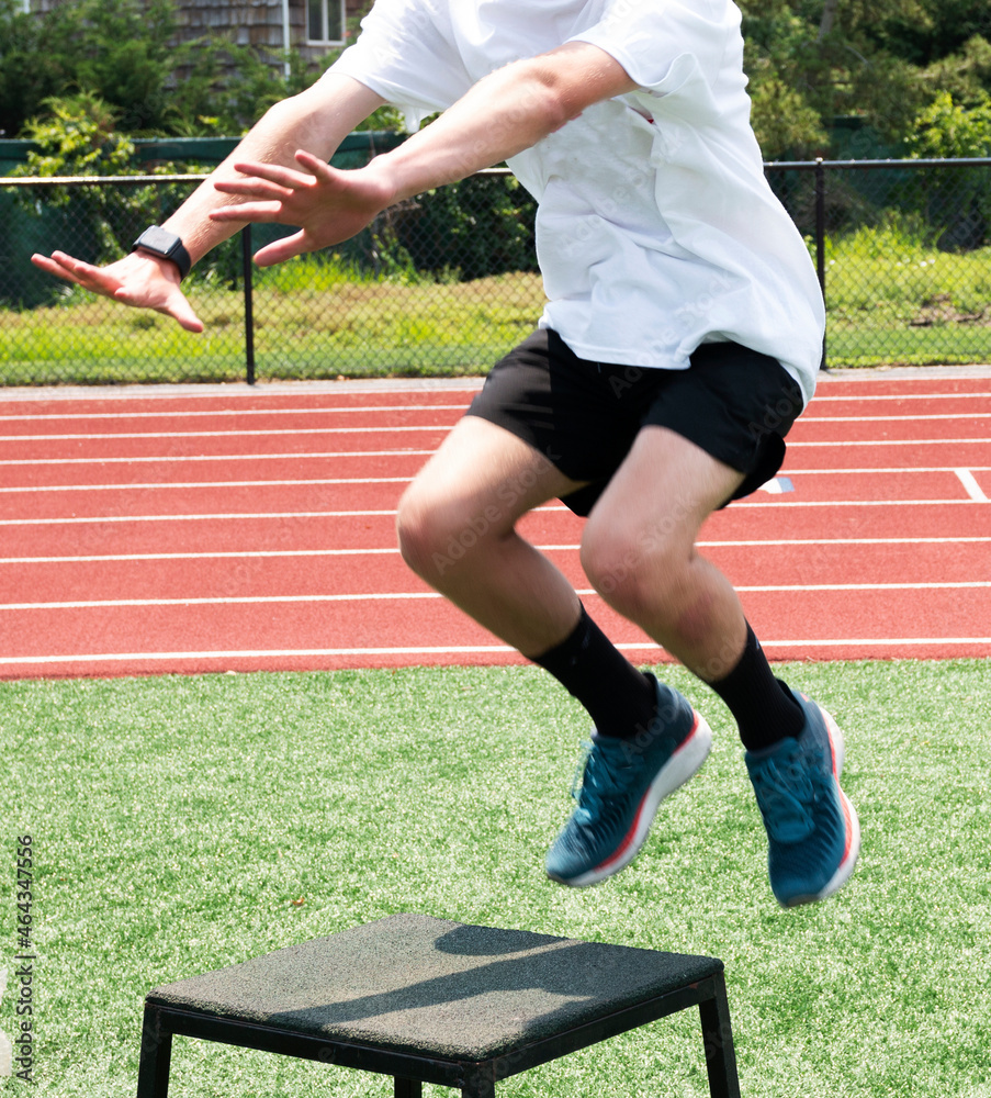 Foto de Teenage boy jumping onto a plyo box outdoors on a turf field do ...
