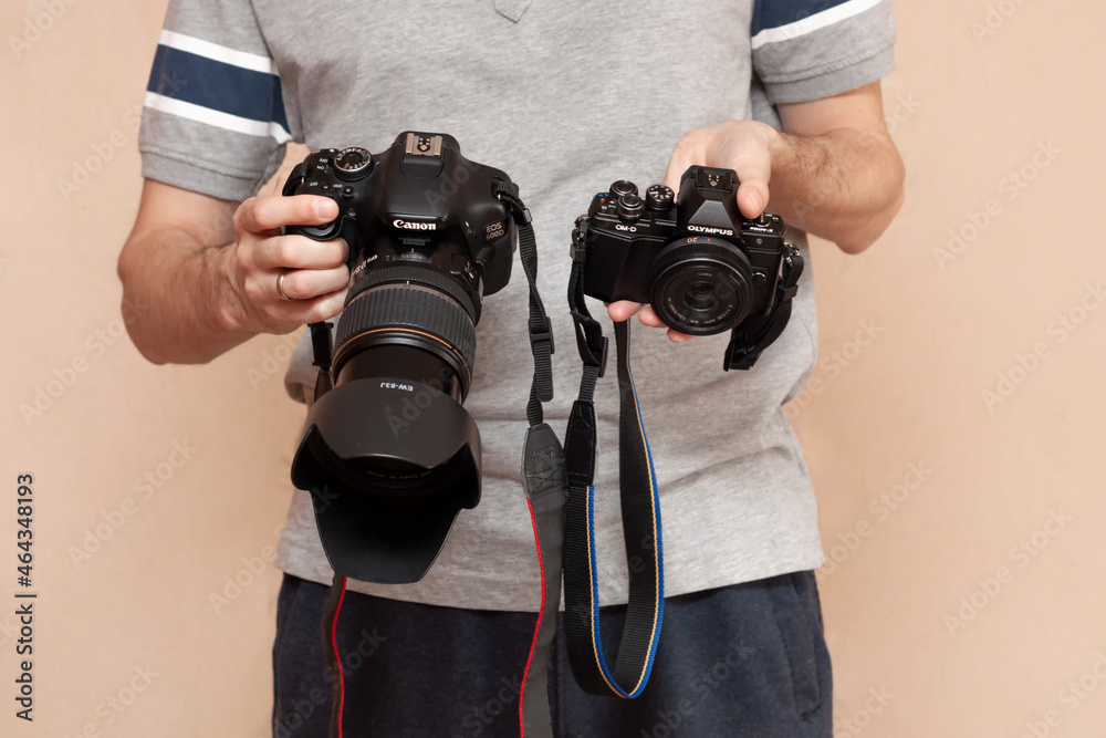 Man is holding in one hand dslr camera Canon and mirrorless Olympus in ...