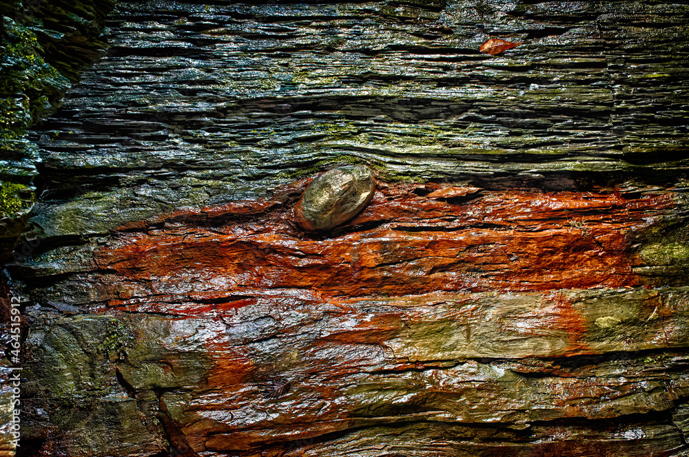 A smooth rounded rock sits between two layers of the sedimentary rock ...
