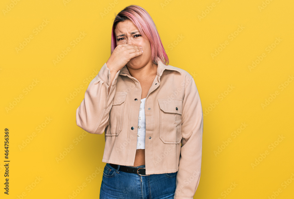 Hispanic woman with pink hair wearing casual clothes smelling something ...