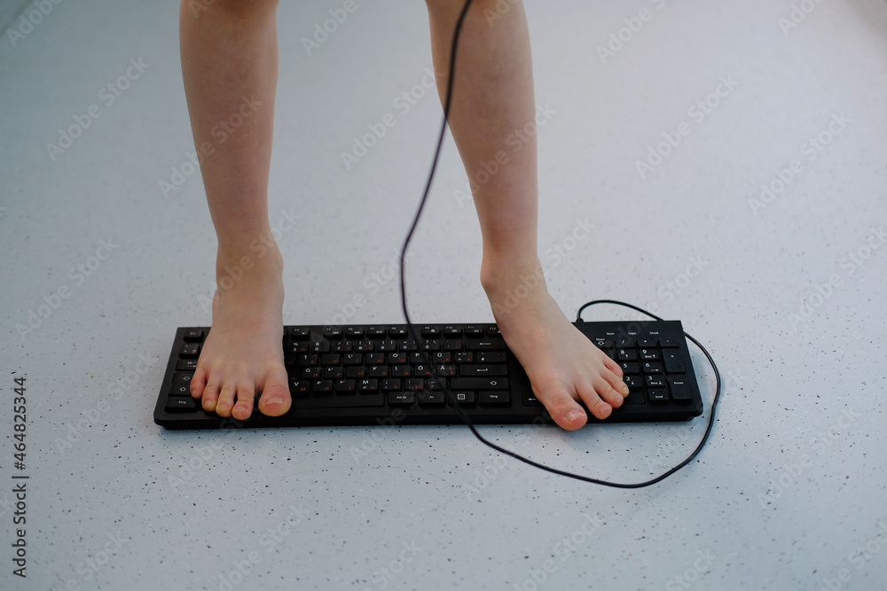 Foto de child stands with his feet on a computer keyboard, presses ...