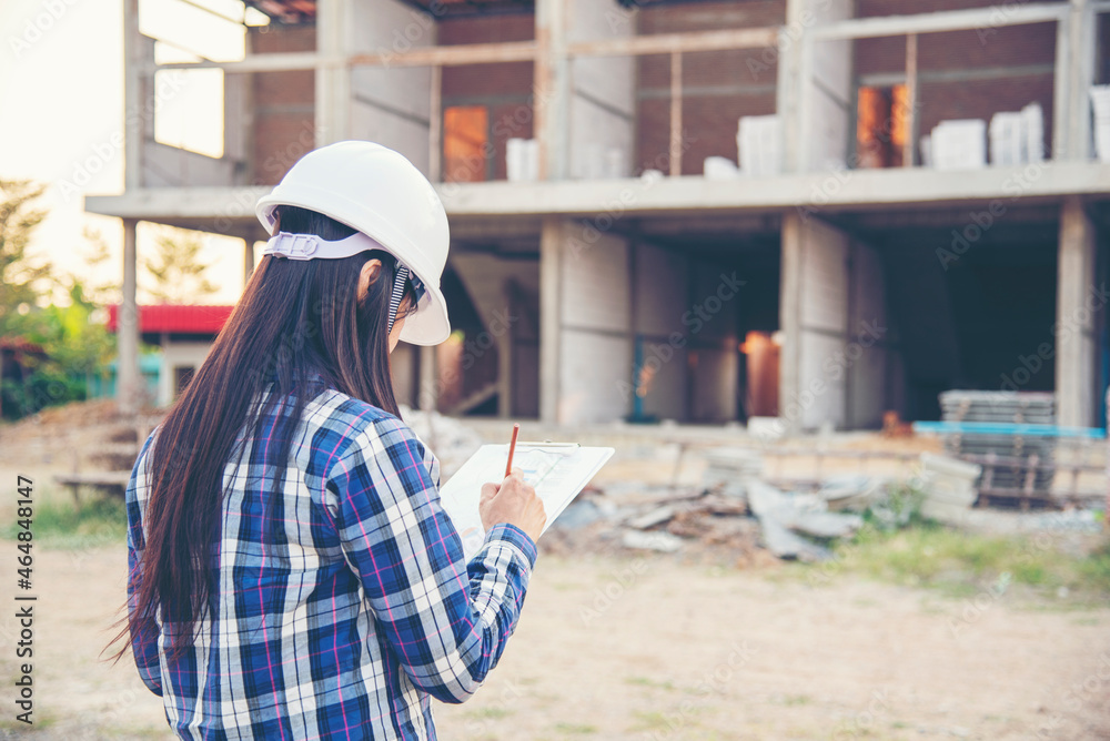 Woman construction engineer writing note wear plaid shirt safety white hard hat at construction ...