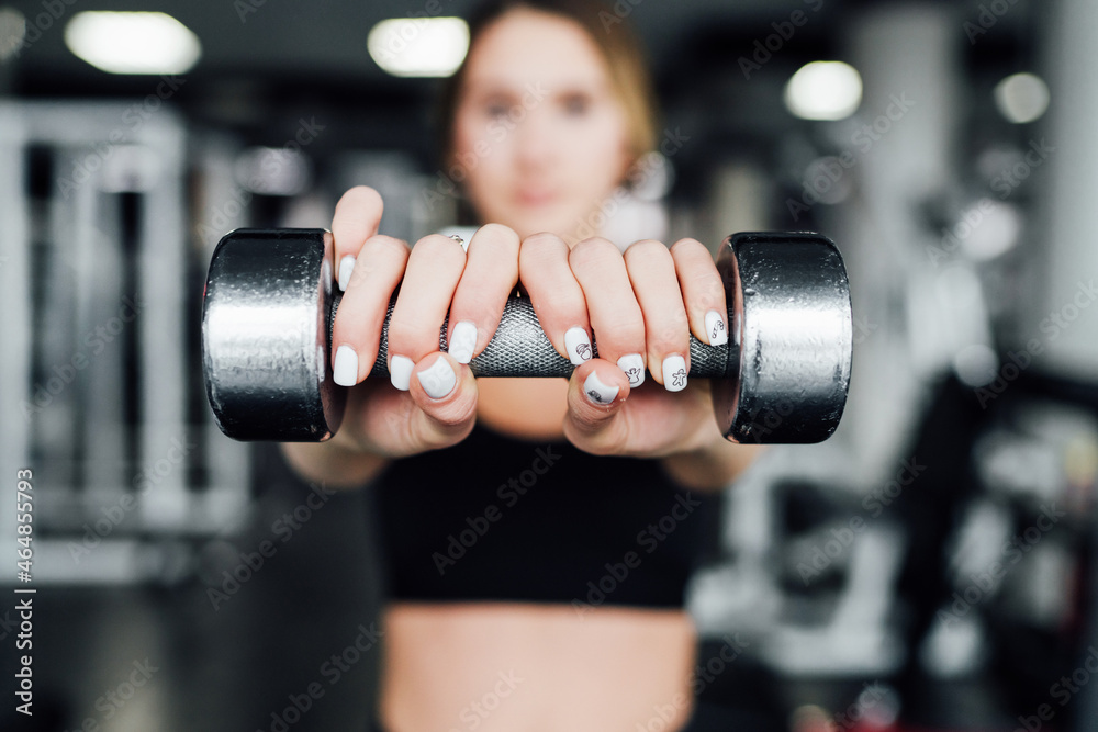 The focus is on the hand of a girl holding a dumbbell and pushing it ...
