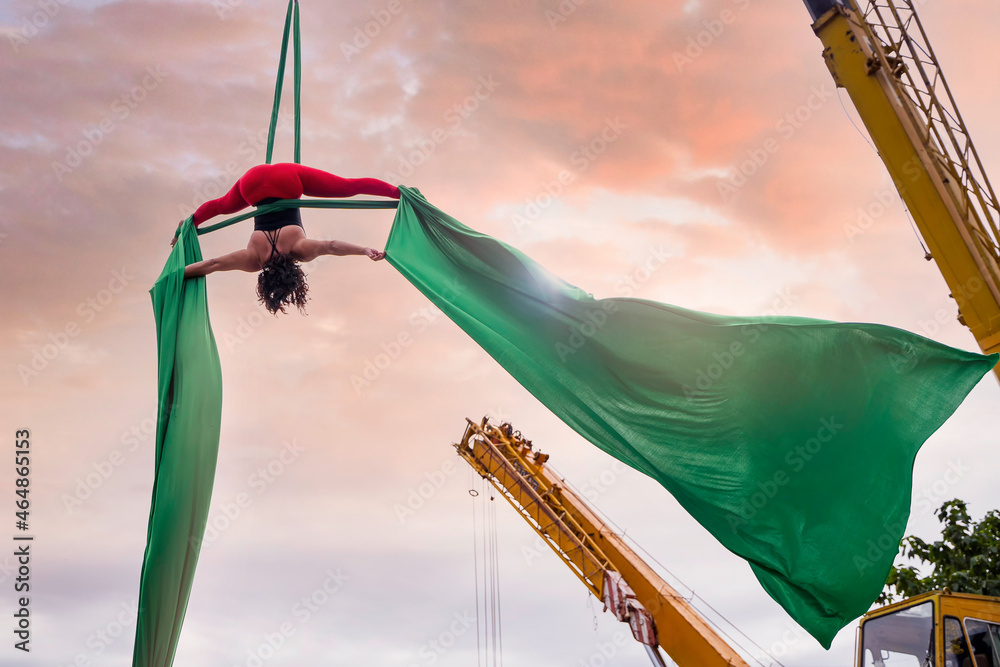 Woman dancing acrobatic with fabric from yellow crane on a sunset sky ...