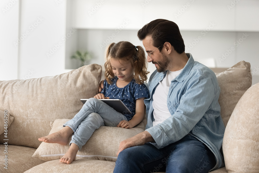 Caring smiling young father in eyeglasses watching happy little ...