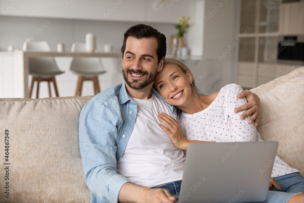 Happy bonding dreamy young family couple sitting on cozy sofa with ...