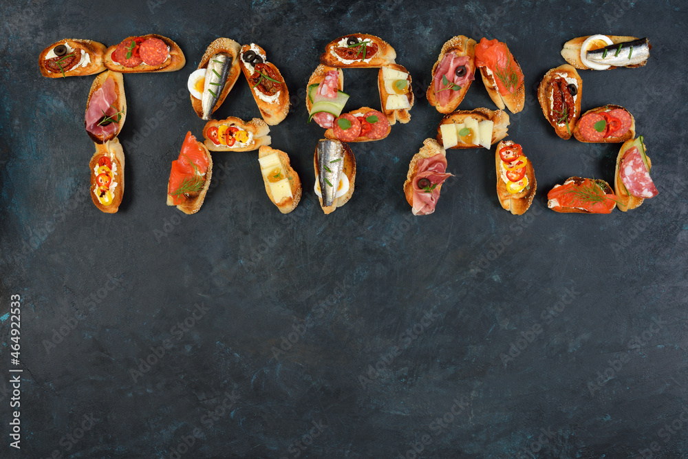 Canapes mit spanischen Spezialitäten als Tapas-Schriftzug auf dunklem ...