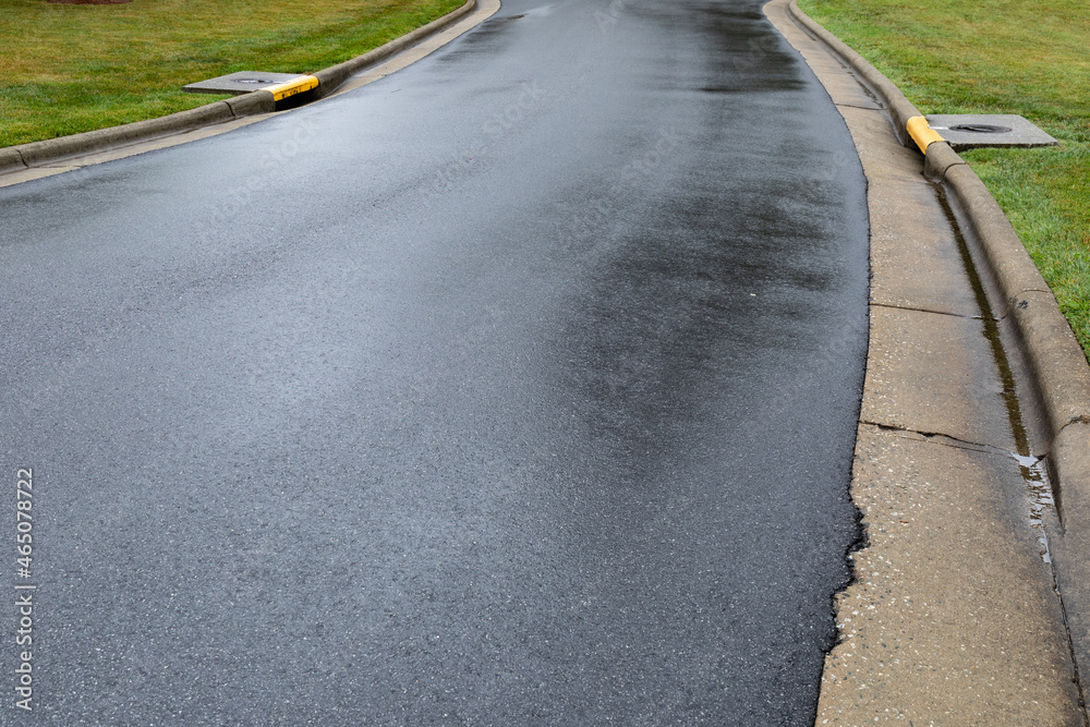 Sweeping asphalt roadway wet from rain, water draining on each side ...