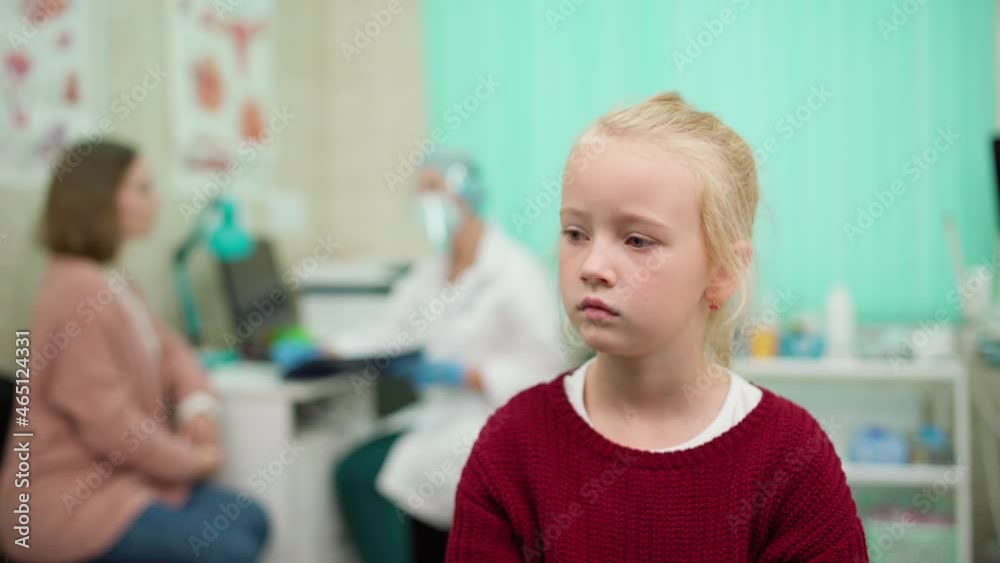 Anxious unhappy little girl waiting in doctors office while her mother ...