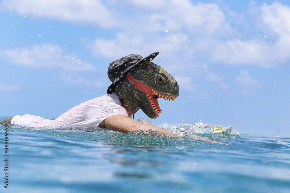 Man wearing dinosaur mask swimming with surfboard in sea Stock Photo ...