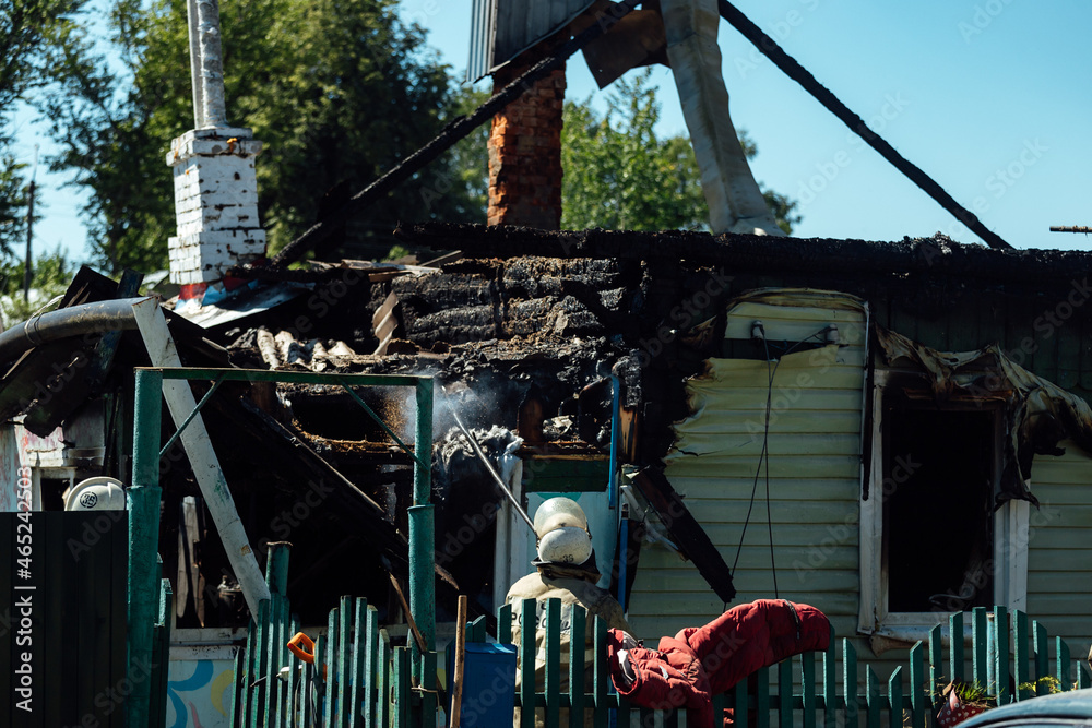 a firefighter pours water on a burned house. the wreckage of a wooden ...