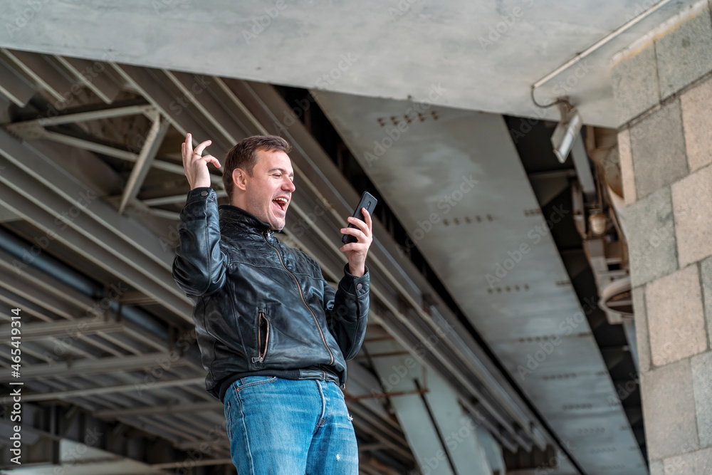 Happy millennial man showing yeah gesture and using smartphone under ...