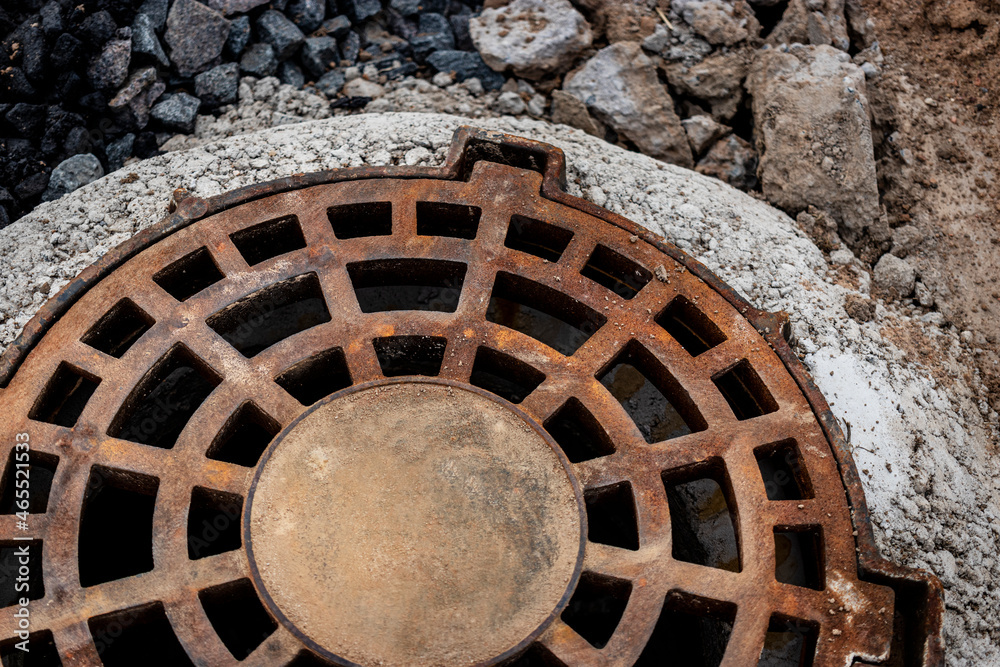 Cast-iron stormwater drainage hatch on the road before asphalt pavement ...
