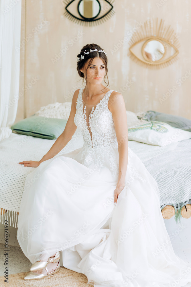 Cute bride in a white dress sitting on the bed in a stylish room. Stock ...