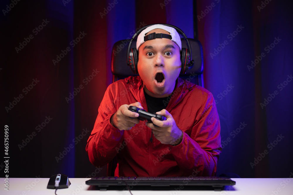 Excited and shocked face of Asian gamer with headphone holding joystick ...
