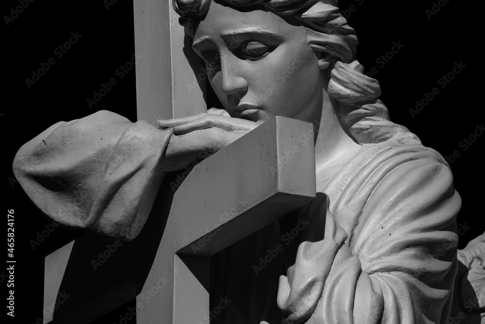 Beautiful sad angel with cross on black background. Fragment of an ...