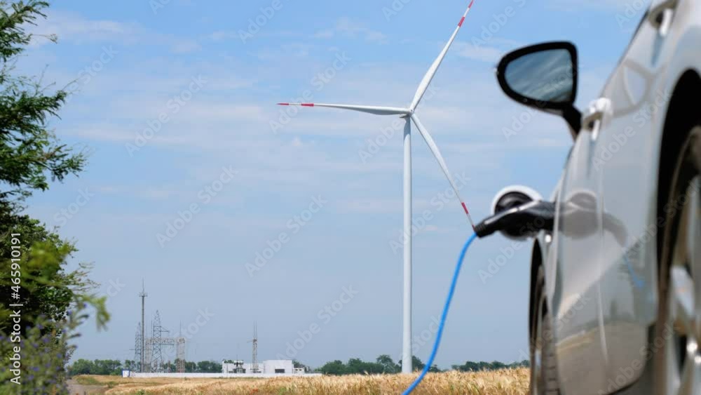 Vidéo Stock Wind turbine charges electric car. White Tesla connected to ...